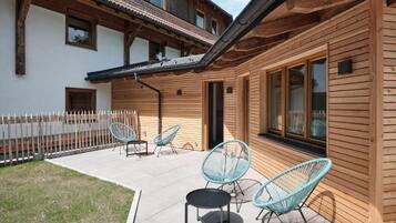 Uma casa de madeira com um espaço de pátio que inclui duas cadeiras e uma mesa.