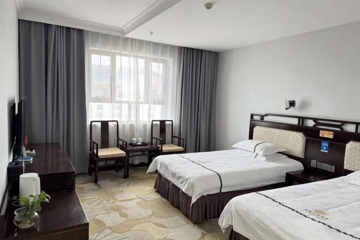 Quarto de hotel com duas camas, uma escrivaninha, uma cadeira e uma televisão.