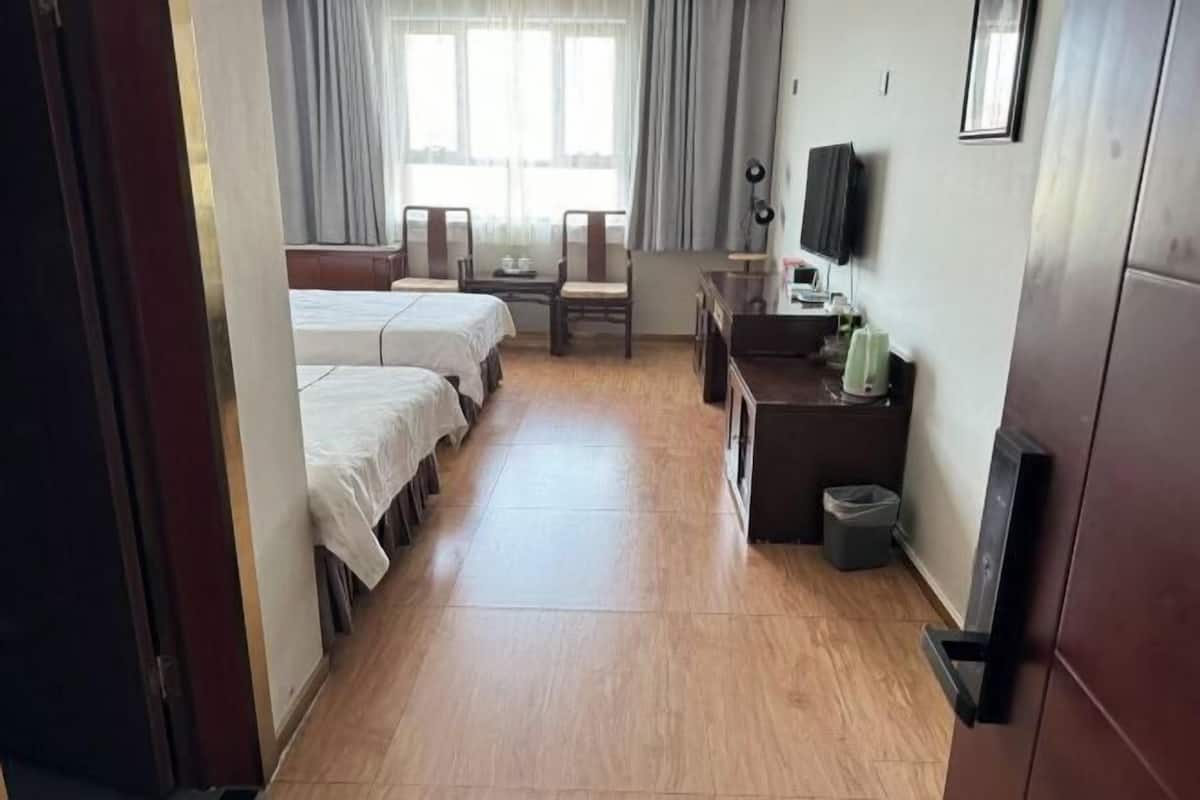 Quarto de hotel com duas camas, uma mesa, uma cadeira, uma televisão e uma janela com cortinas.
