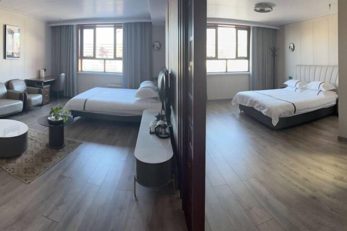 Quarto de hotel com duas camas, uma escrivaninha, uma cadeira, uma mesinha e um vaso de planta.