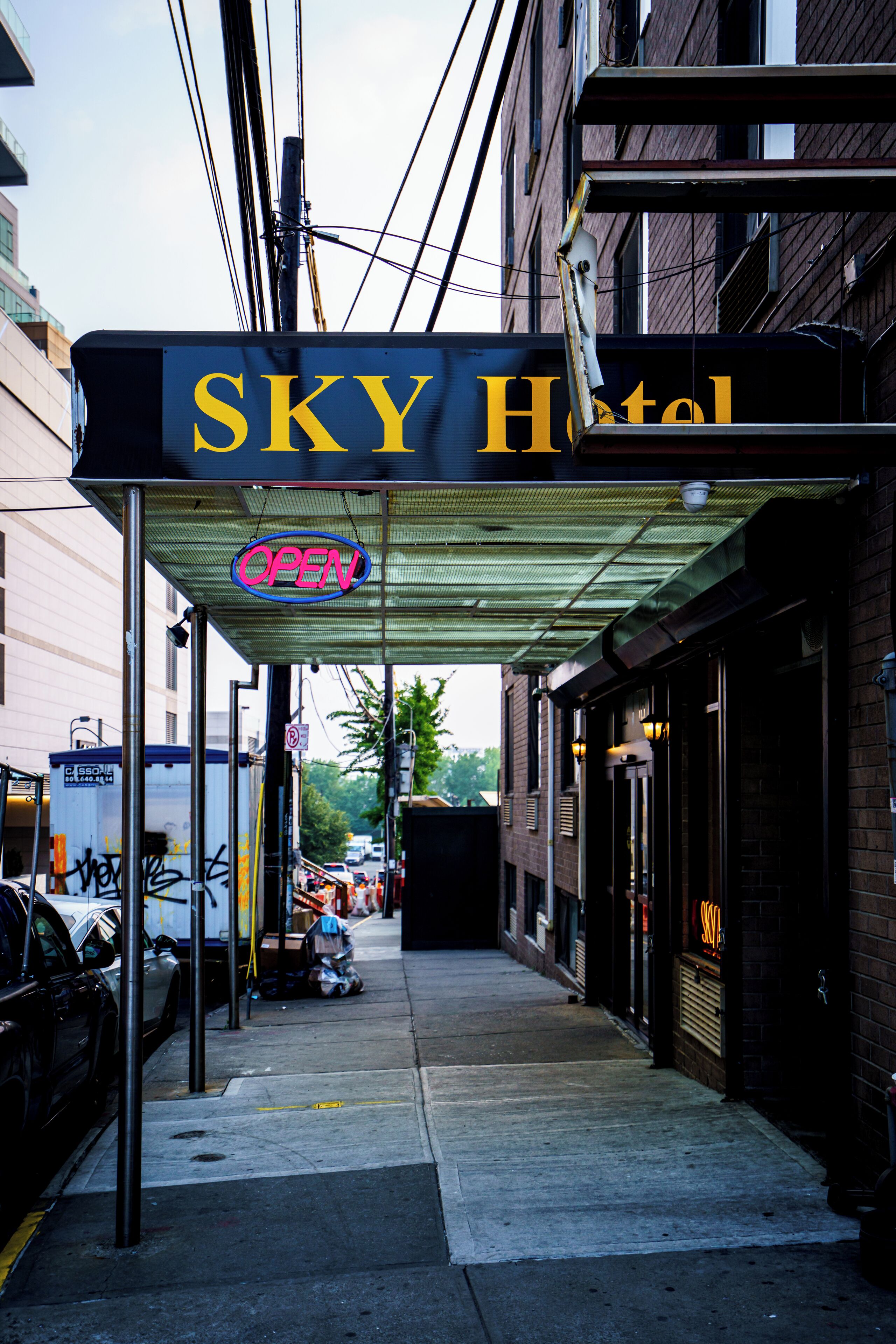 Entrada de um hotel com uma placa indicando "SKY Hotel" e um aviso de "ABERTO".