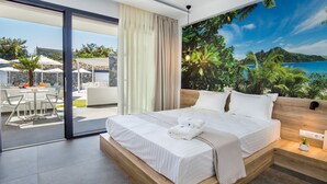 Quarto moderno com uma cama grande, vista para o exterior e área de jantar com guarda-sóis.