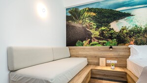 Quarto moderno com cabeceira de madeira, sofá bege, mesa de cabeceira pequena com uma planta e um grande mural com uma paisagem de praia tropical.