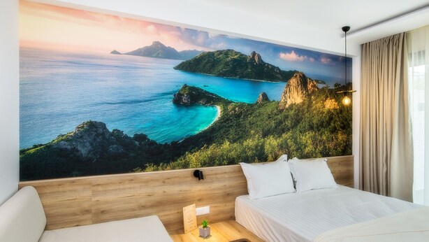 Quarto com um grande mural de paisagem costeira, cabeceira de madeira, duas camas, mesa de cabeceira com abajur e janela com cortinas.