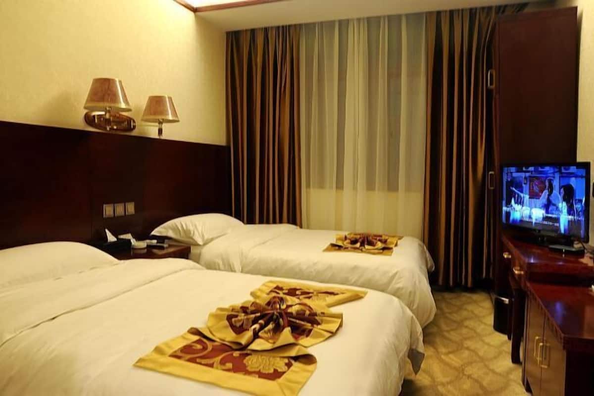 Quarto de hotel com duas camas, uma televisão e uma cortina.