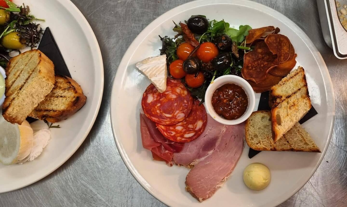 Duas travessas de comida com pães, queijos, salame, azeitonas e uma salada.