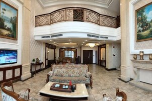 Um hall espaçoso com teto alto, balaustrada ornamentada e área de estar central com sofá e poltronas.