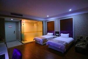 Quarto de hotel com duas camas, porta de vidro, uma cadeira roxa e uma mesa pequena.
