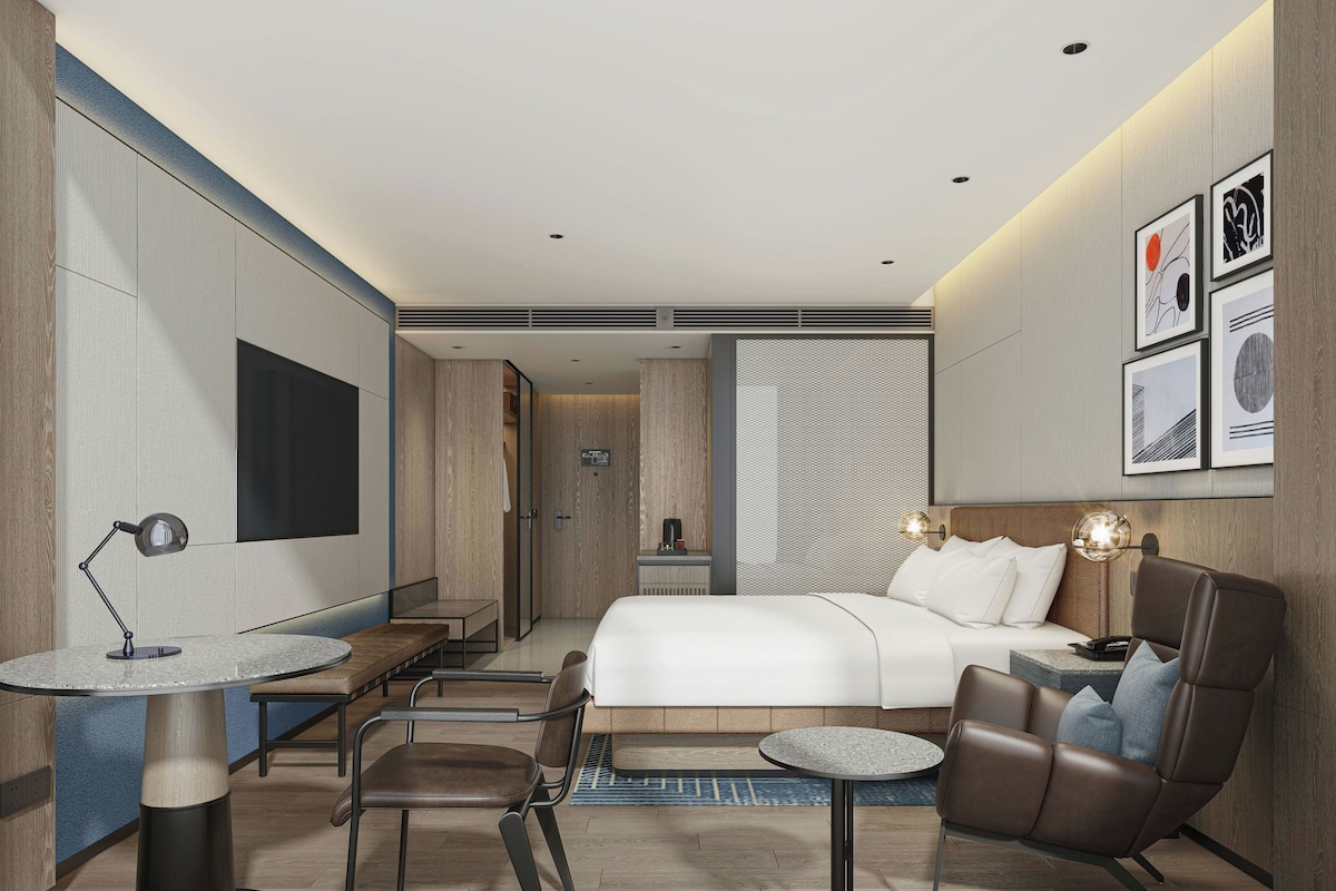 Quarto de hotel moderno com cama, escrivaninha, cadeira e obras de arte nas paredes.