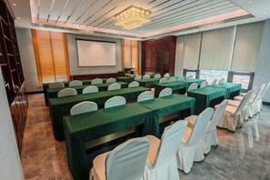 Uma sala de conferências com várias mesas e cadeiras, uma tela de projetor e uma janela grande com persianas.