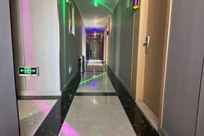 Corredor de hotel com piso refletivo, placas de sinalização e uma porta à direita.