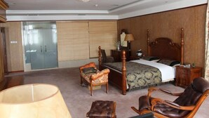 Um quarto espaçoso com cama de dossel, uma área de estar com poltronas e uma janela grande.