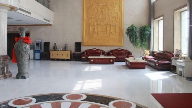 Um hall espaçoso com teto alto, uma grande escultura em relevo de madeira, sofás de couro e piso de mármore.