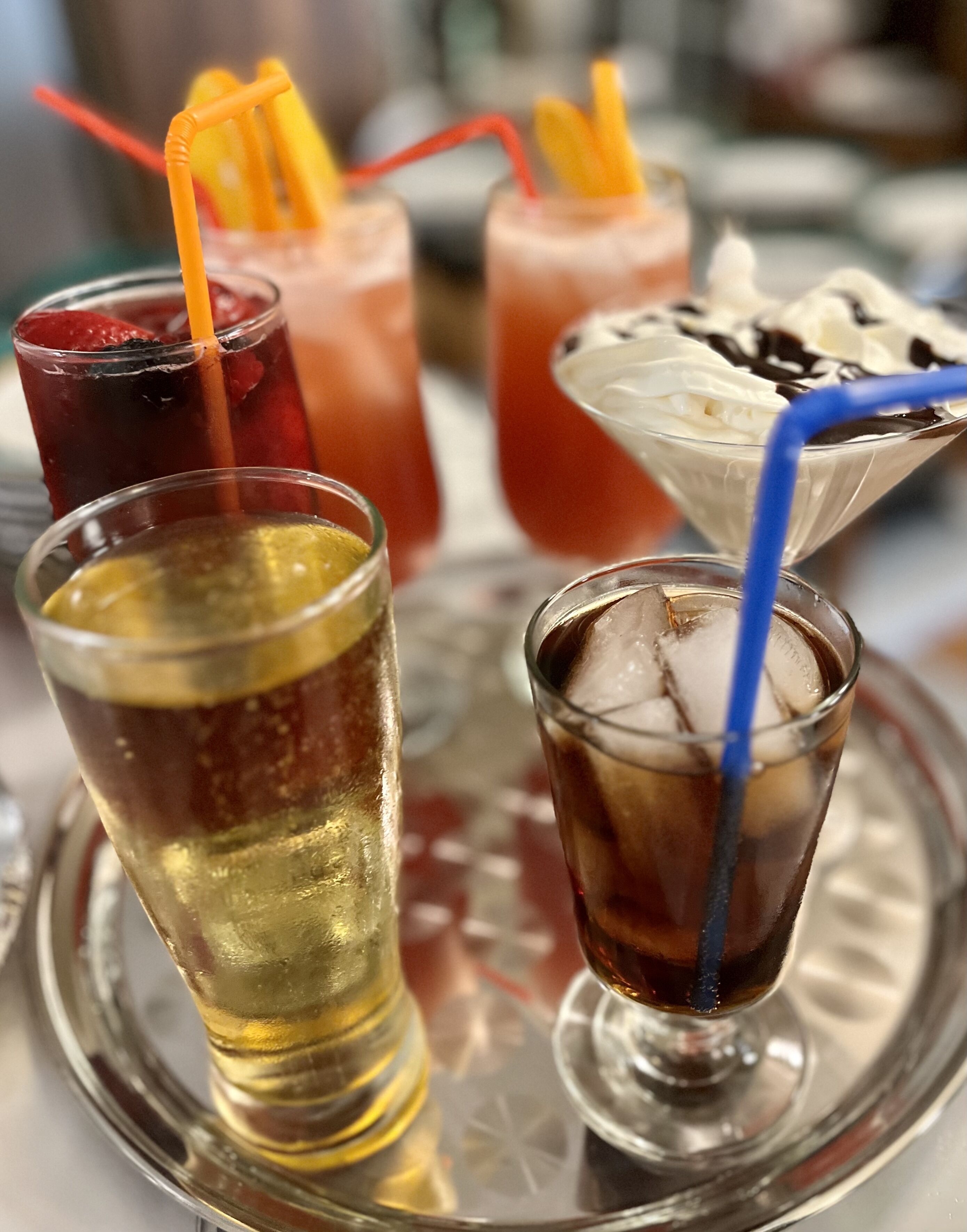 Uma bandeja com diversas bebidas, incluindo chá gelado, limonada e um coquetel com canudo azul.