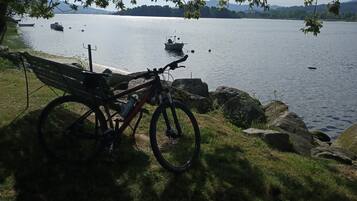 Uma bicicleta estacionada em área gramada à beira do lago, com um banco e pedras por perto.