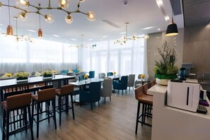 Uma sala de jantar moderna com uma mesa comprida, várias cadeiras, iluminação pendente e bancada de cozinha.