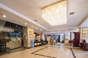Um saguão de hotel com balcão de recepção, um lustre e uma janela grande.