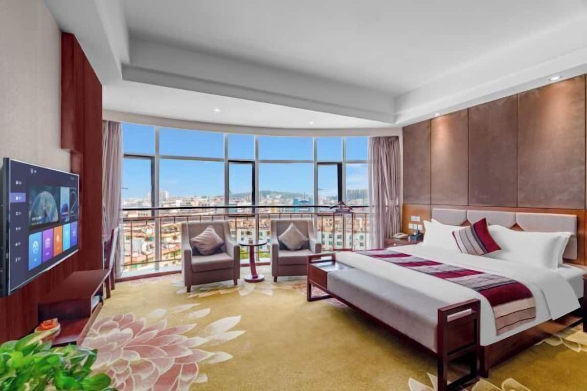 Quarto de hotel com uma cama grande, televisão e varanda com vista para a cidade.