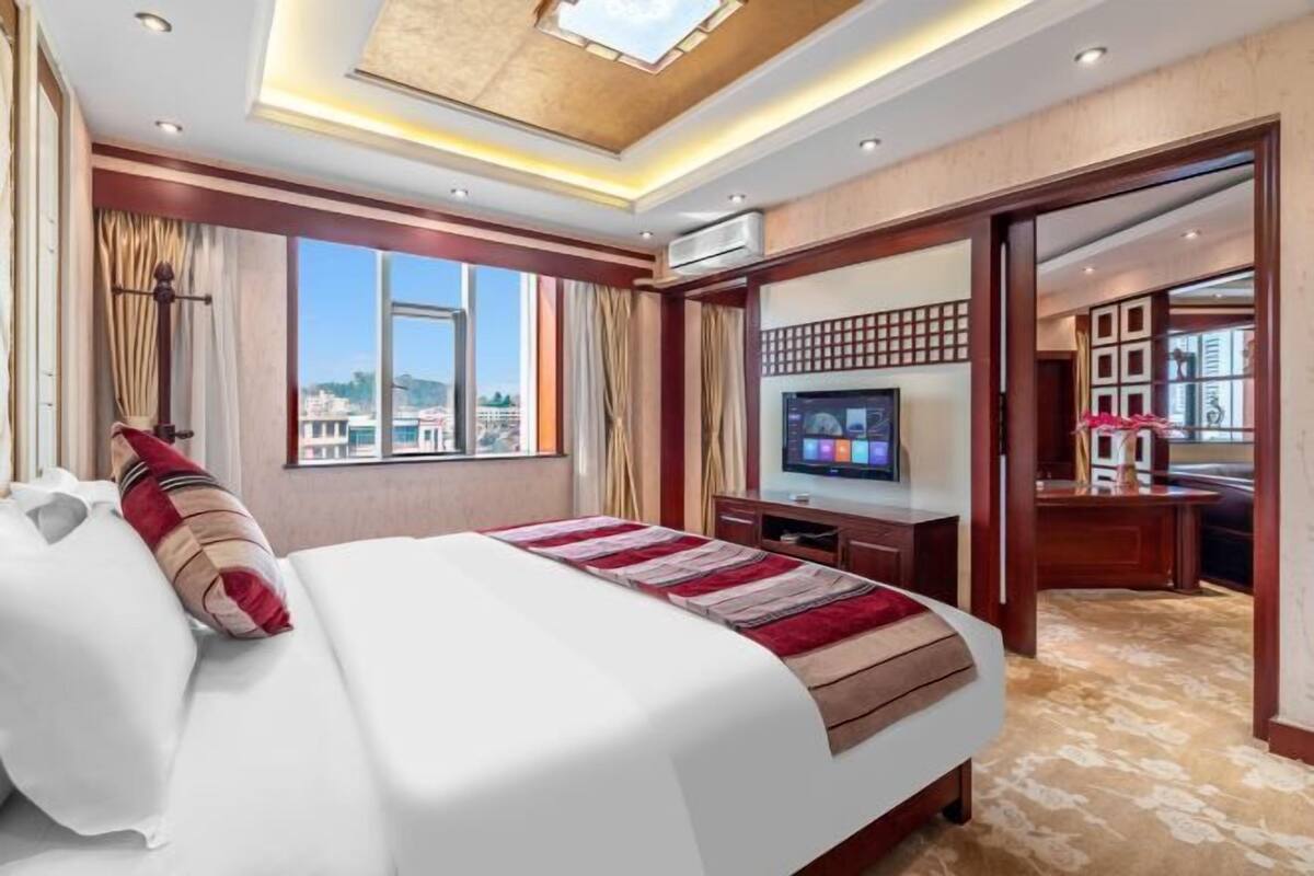 Quarto de hotel com uma cama grande, uma escrivaninha, televisão e vista para a cidade.