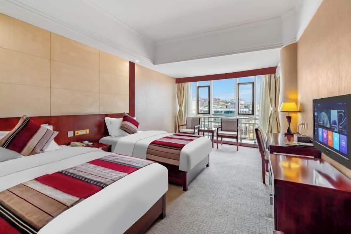 Quarto de hotel com duas camas, uma escrivaninha, uma cadeira e uma televisão.