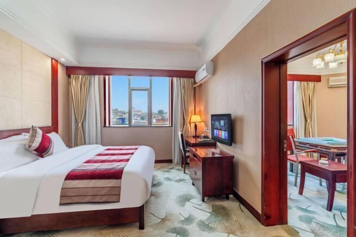 Quarto de hotel com uma cama, uma escrivaninha, uma televisão e vista para a cidade pela janela.