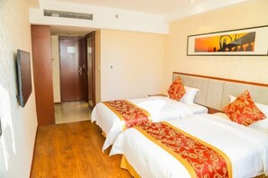 Quarto de hotel com duas camas, piso de madeira, um quadro na parede e uma porta que dá para outro cômodo.