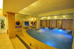 Uma grande piscina coberta com design curvo, rodeada por paredes com padrões texturizados e teto com iluminação embutida.