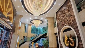 Um hall imponente com uma escadaria central, um grande lustre e uma parede decorativa com um relevo escultórico.