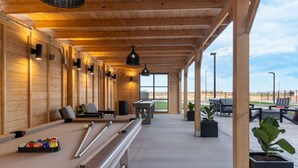 Uma mesa de bilhar com taco, um espaço de estar com cadeiras e vista para o exterior.