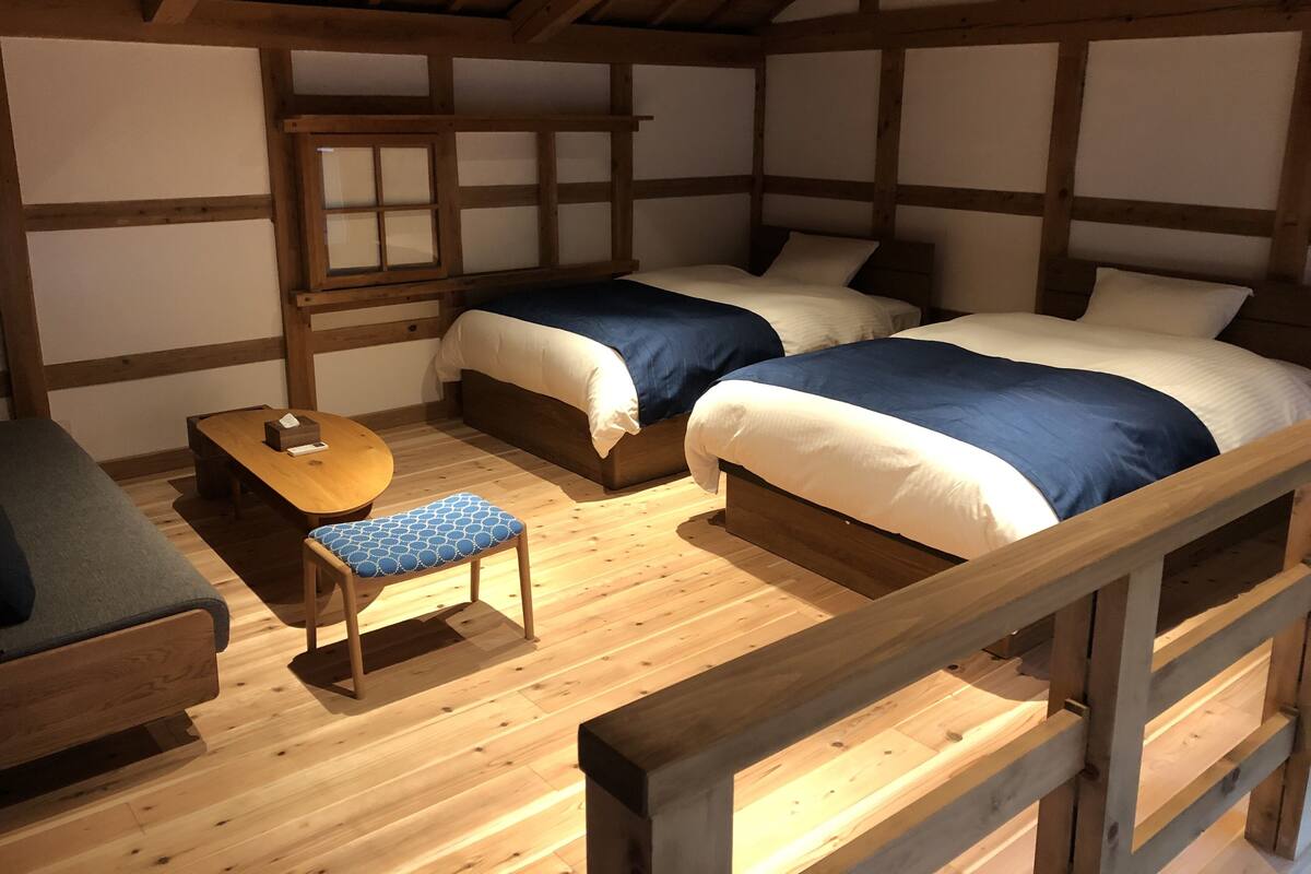 Um quarto aconchegante com duas camas, uma mesinha e um banco.