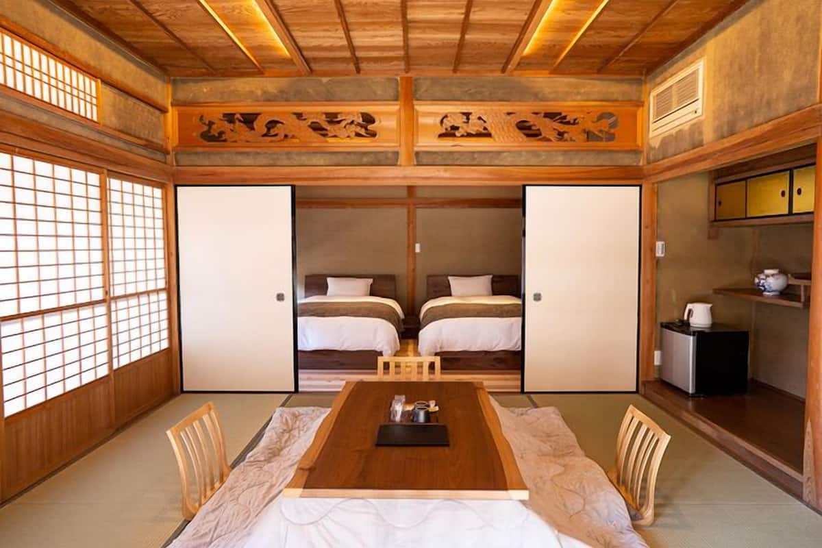 Quarto tradicional em estilo japonês, com piso de tatame, duas camas, uma mesa de madeira com bandeja e portas deslizantes.