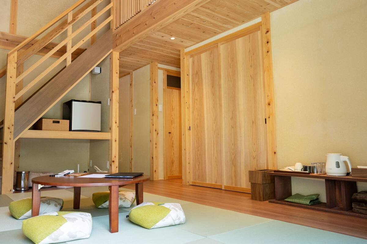 Um quarto com escada de madeira, mesa com almofadas e chaleira sobre uma mesinha.