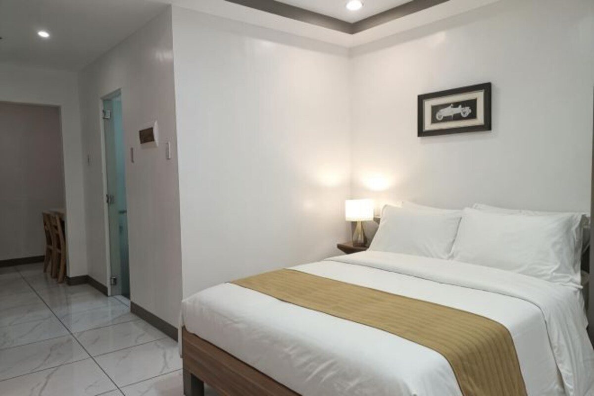 Quarto de hotel com cama, mesa de cabeceira, abajur e um quadro na parede.