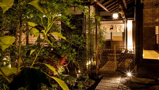 Um jardim japonês tradicional, com um caminho de pedra que leva a um portão de madeira.