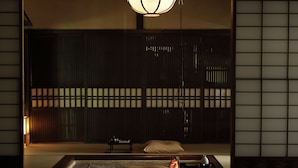 Um quarto japonês tradicional com tatames, uma mesa baixa com uma vela, luminária pendente e uma porta deslizante com padrão quadriculado.