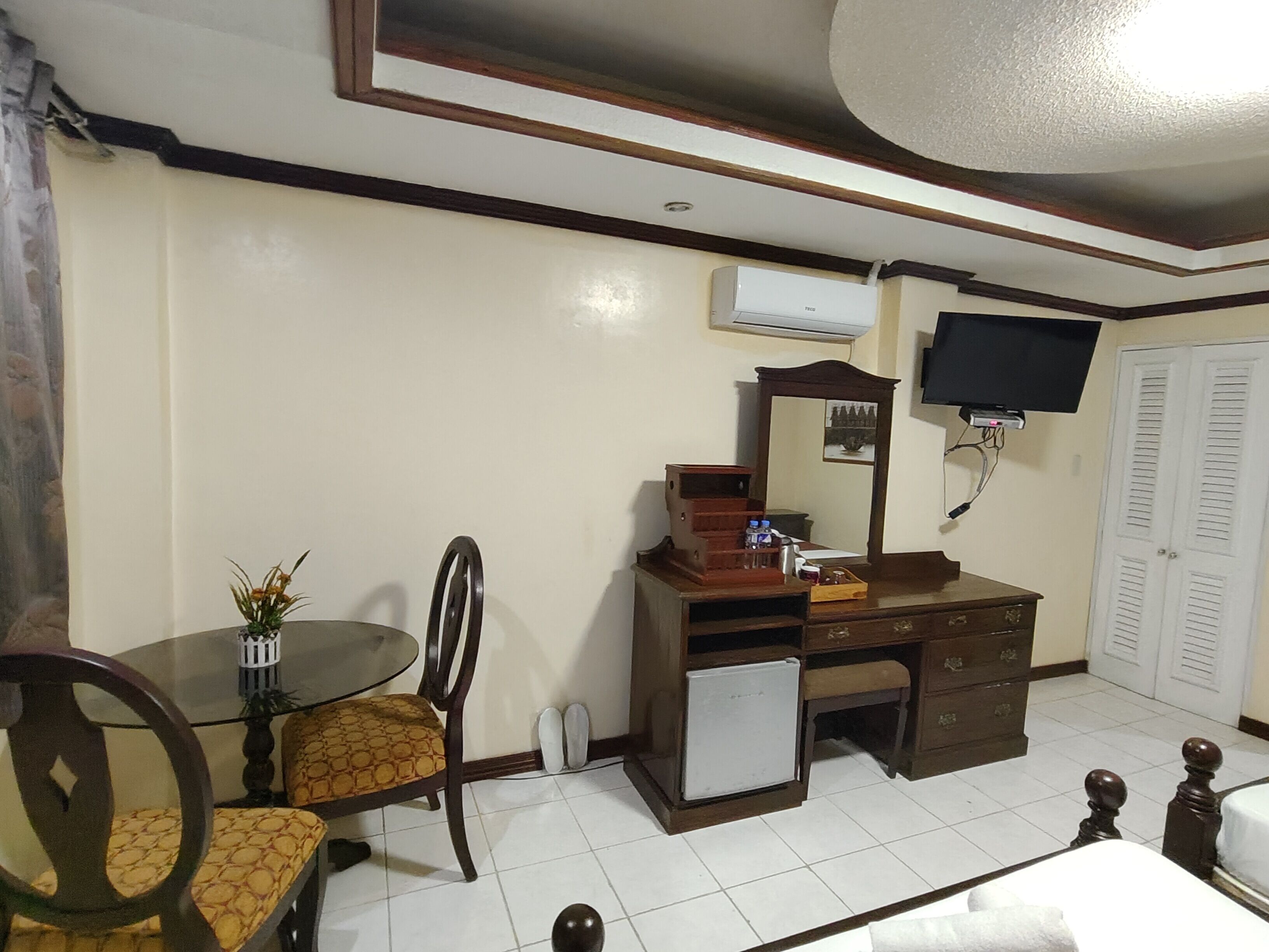 Quarto de hotel com uma cama, uma escrivaninha com espelho, televisão e um pequeno frigorífico.
