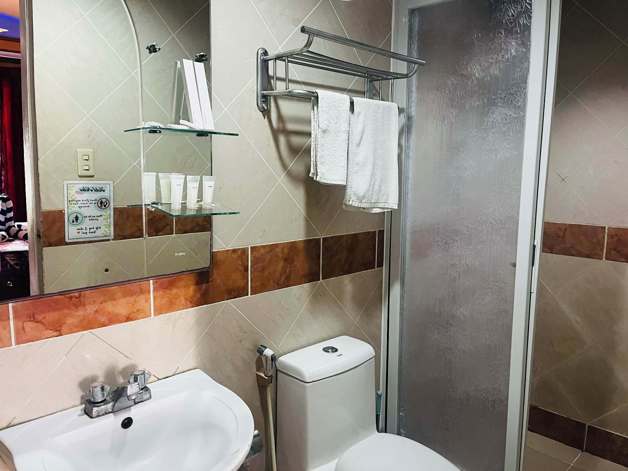 Uma casa de banho com lavatório, sanita e chuveiro. Há toalhas e produtos de higiene na parede.