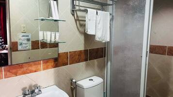 Uma casa de banho com lavatório, sanita e chuveiro. Há toalhas e produtos de higiene na parede.