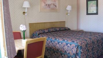 Quarto de hotel com uma cama, duas luminárias de cabeceira, um quadro na parede, uma mesinha com um vaso de flores e uma cadeira.