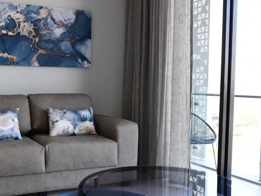 Uma sala de estar moderna com um sofá cinza, duas almofadas decorativas, uma grande pintura abstrata e uma mesa de vidro.