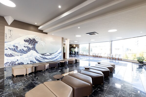Um hall de hotel moderno com uma grande pintura de ondas, assentos confortáveis e vista através de janelas amplas.