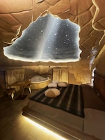 Um quarto com cama, almofadas, uma mesinha e uma cadeira.