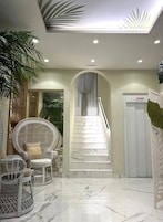 Um interior moderno com escadaria de mármore, móveis de vime e teto com motivos de folhas.