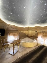 Quarto com teto estrelado, banheira redonda e mesa de jantar com cadeiras.