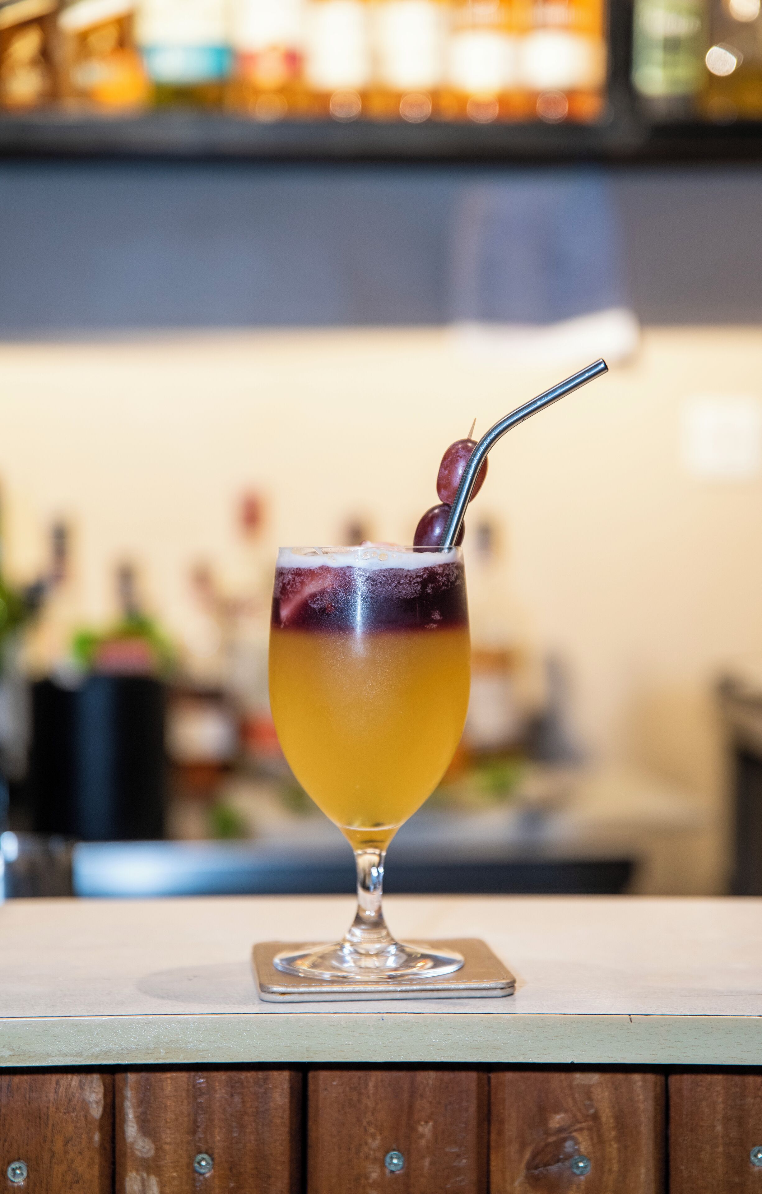 Um copo de cocktail com canudo e cereja sobre um balcão de bar.