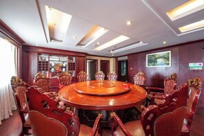 Uma sala de conferências com uma mesa redonda, cadeiras estofadas em vermelho e uma grande janela.