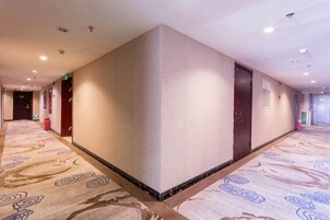 Corredor de hotel com carpete estampado, uma porta e um painel com interruptor de luz.