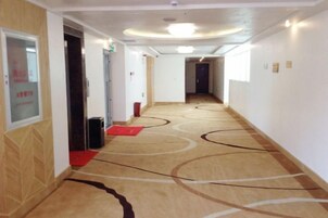 Corredor de hotel com carpete estampado, portas e um cesto de lixo.