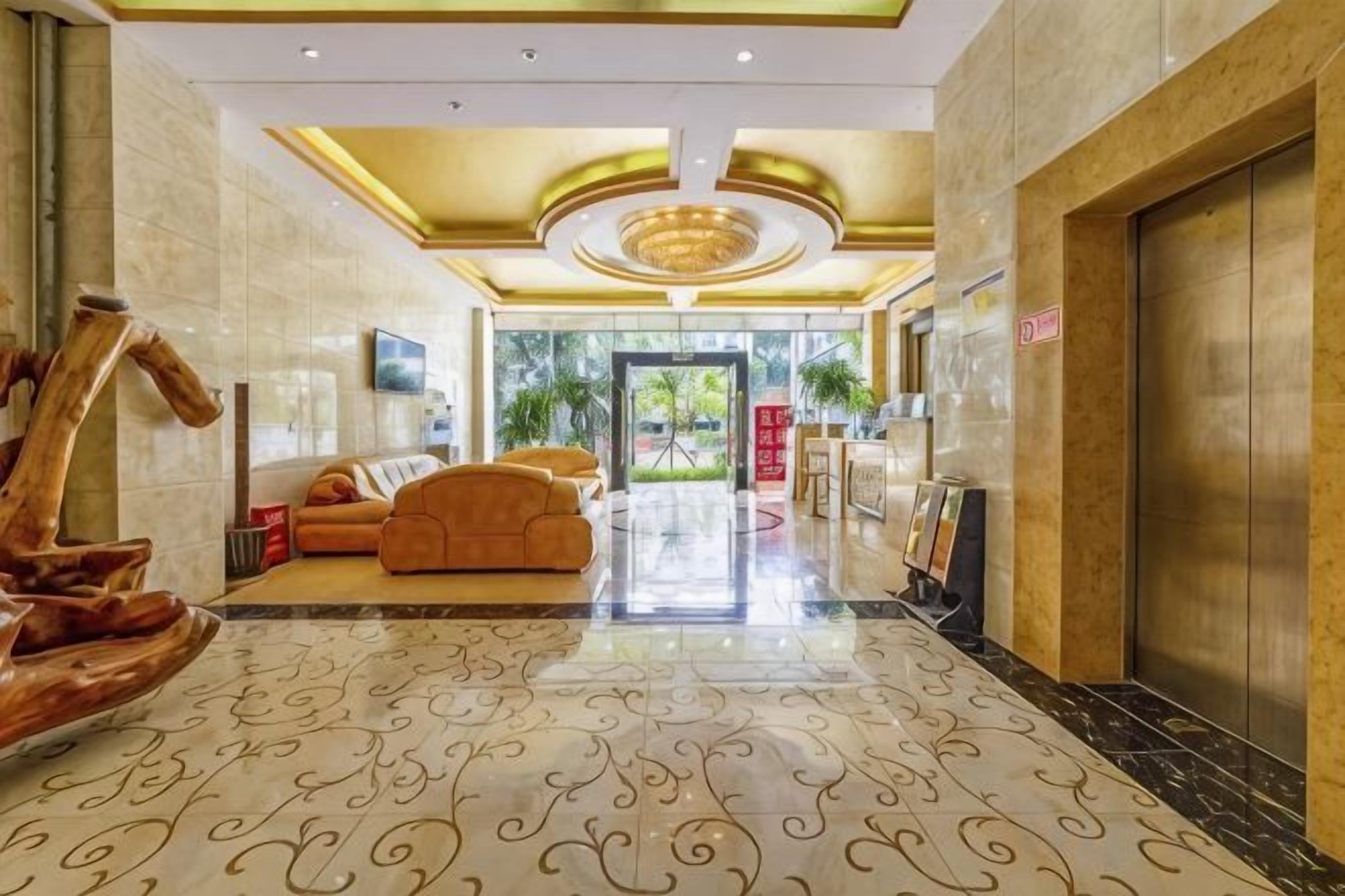 Um saguão de hotel com balcão de recepção, um sofá, uma escultura de madeira e um elevador grande.
