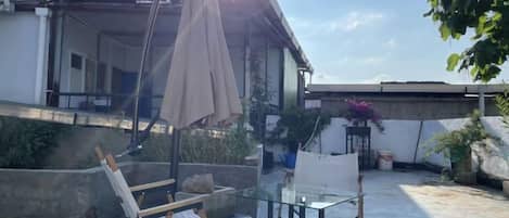 Terraço no telhado com mesa de vidro, cadeira dobrável e um grande guarda-sol.